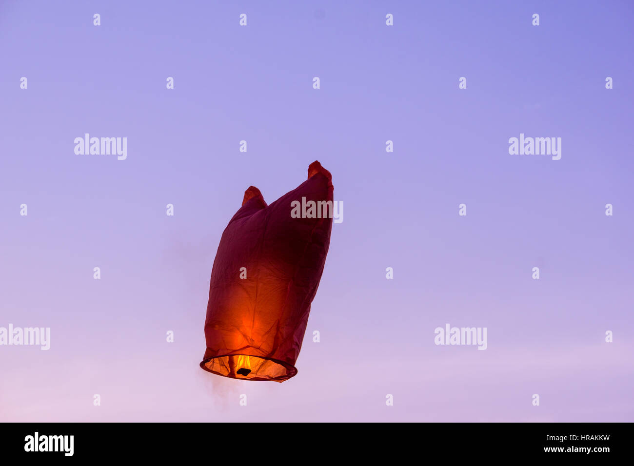 Red sky lantern flying against a blue sky with the flames showing ...