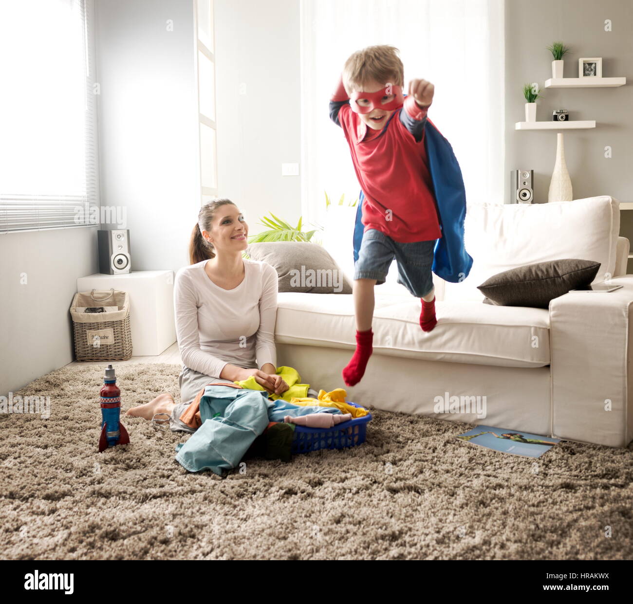 Superhero boy and his mother doing laundry together in the living room ...