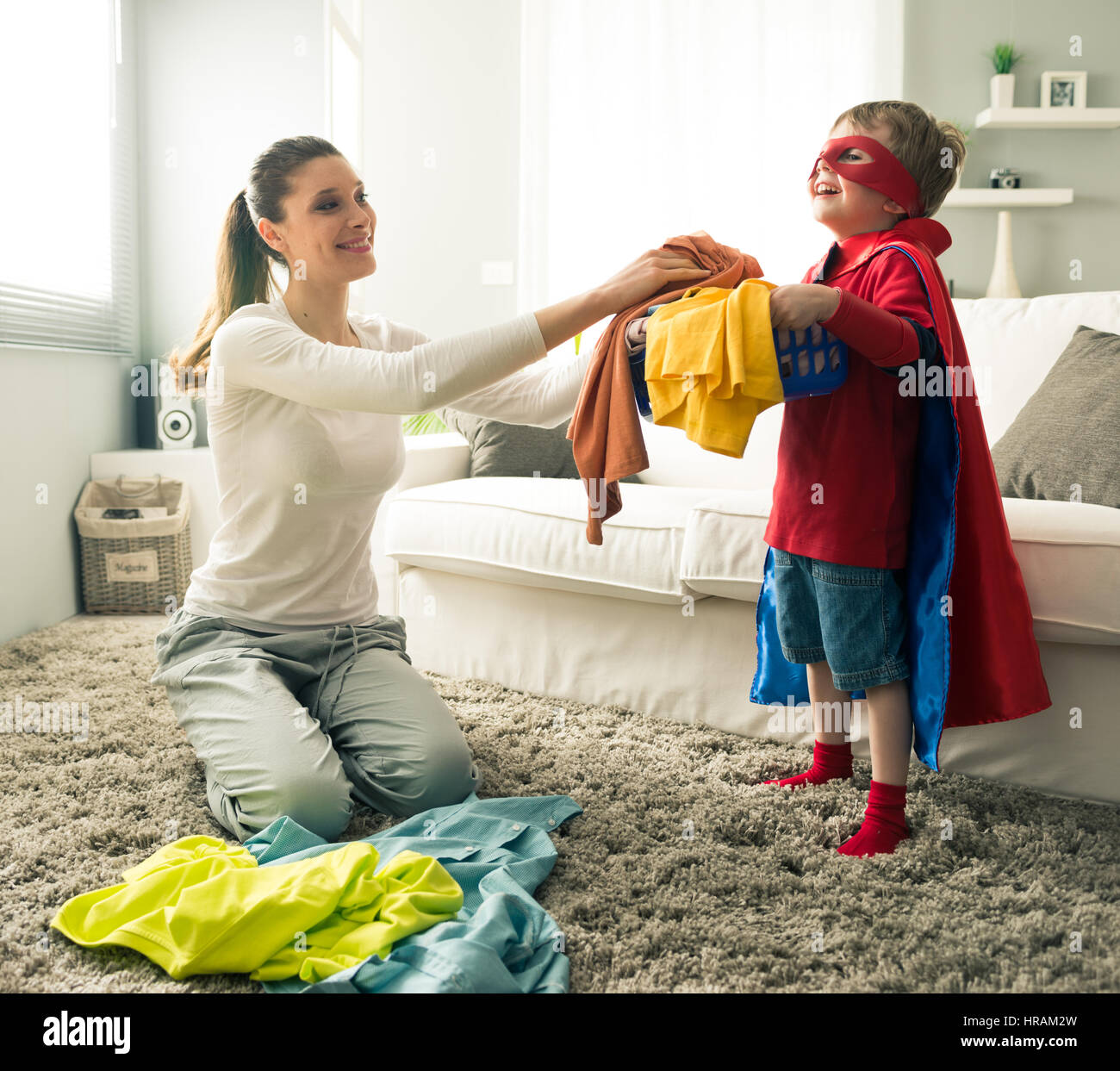 Superhero boy and his mother doing laundry together in the living room ...