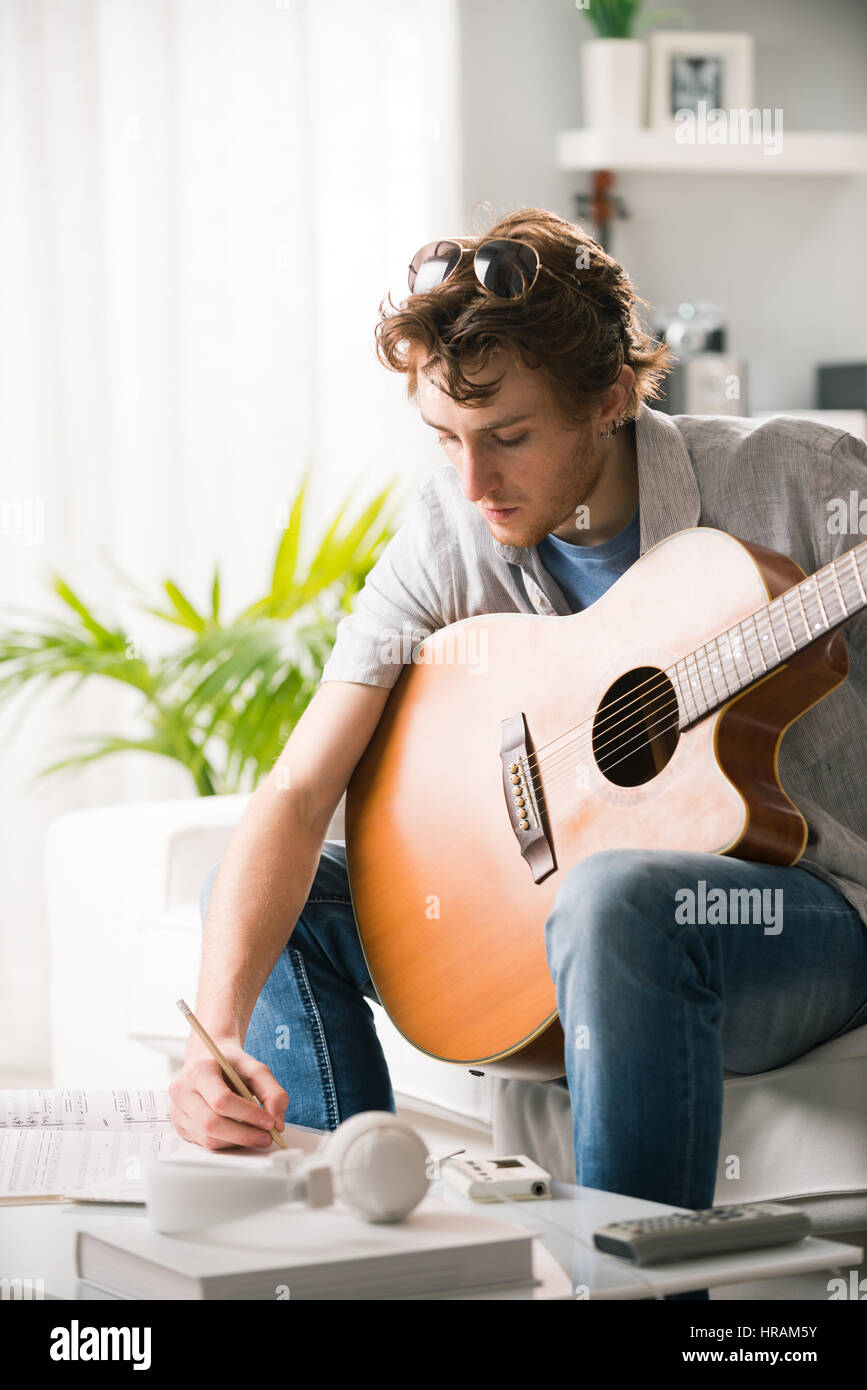 Young man playing guitar and composing a song sitting on sofa Stock ...