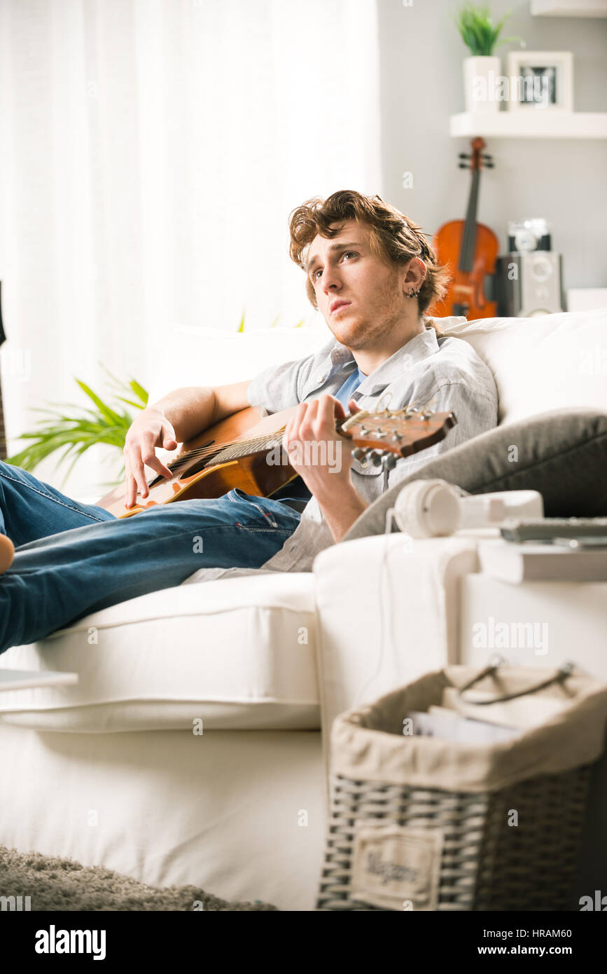Young man playing guitar and composing a song sitting on sofa Stock ...