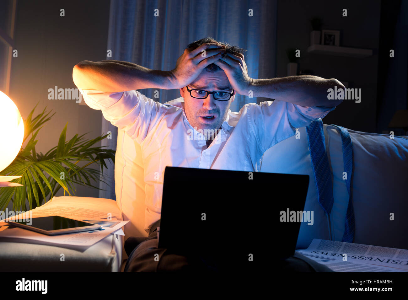 Shocked businessman with head in hands staring at laptop screen late at ...