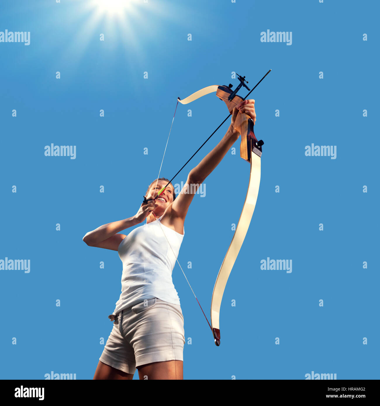 Attractive woman aiming with bow and arrow with blue sky on background ...
