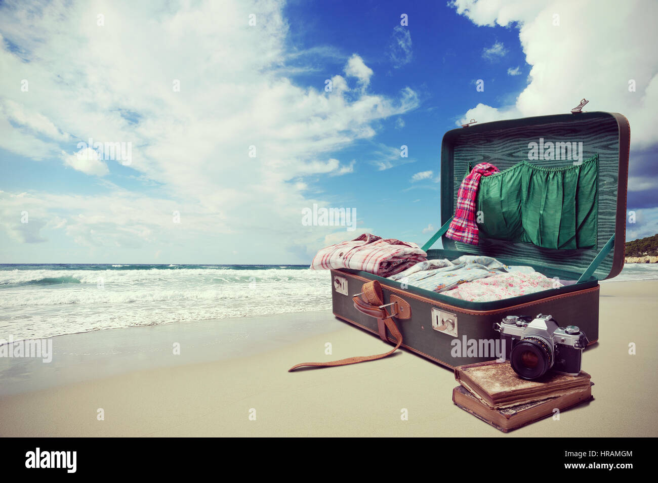 Open suitcase with old books and camera with seaside and blue sky on ...