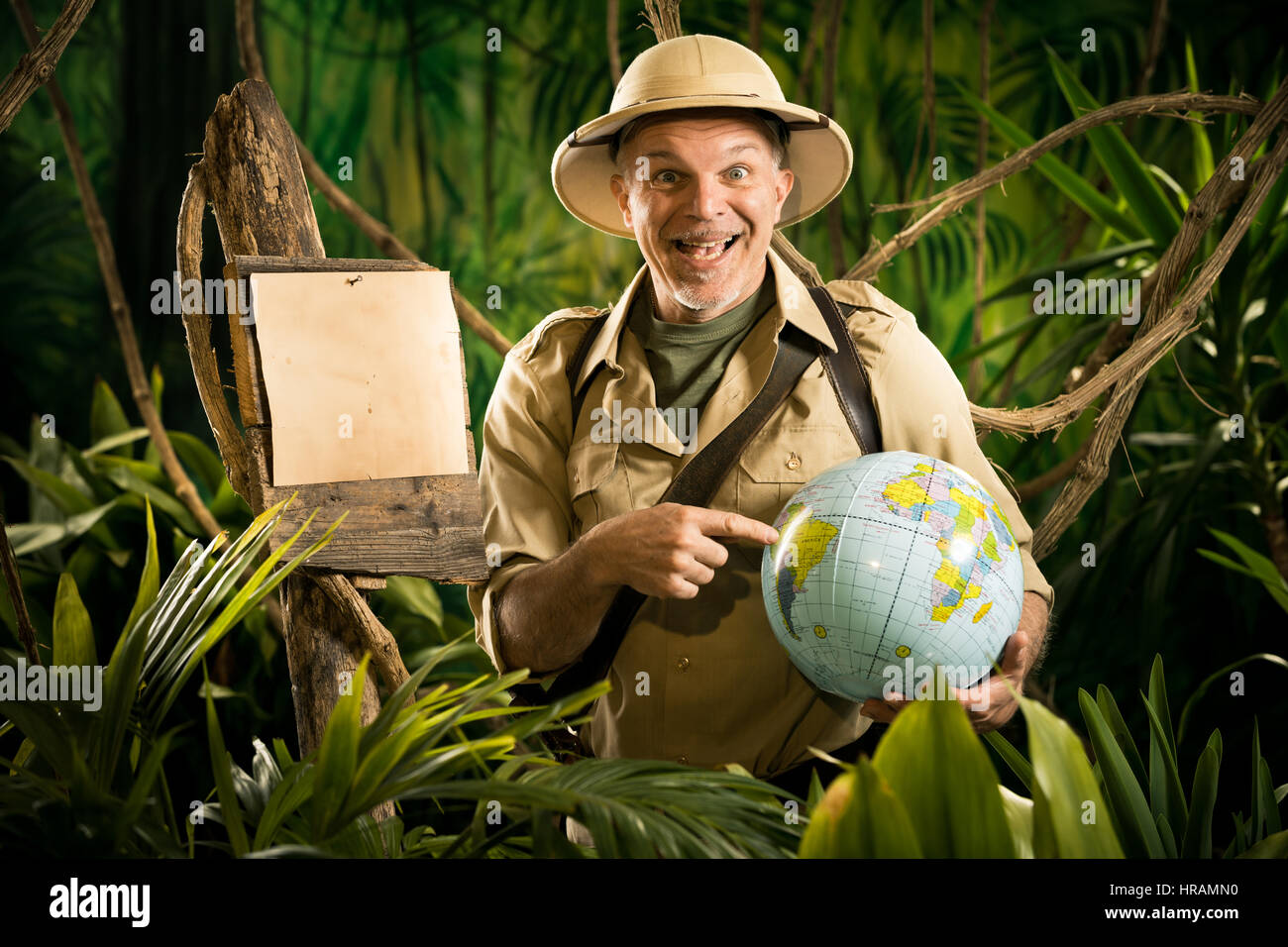 Cheerful explorer in the jungle pointing to a globe next to a wooden ...