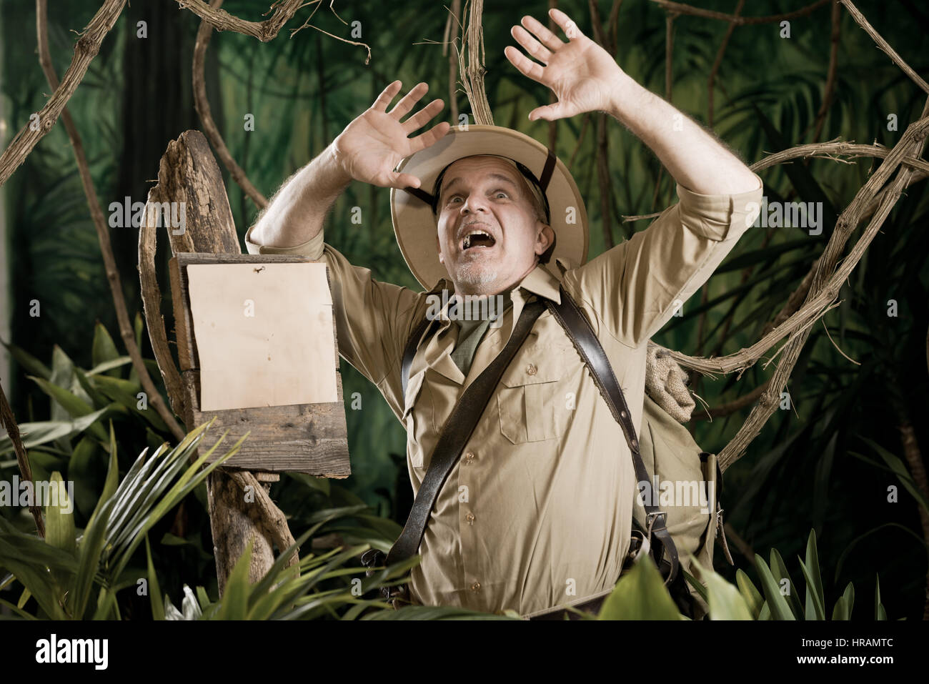 Terrified explorer in the jungle with arms raised looking up and ...