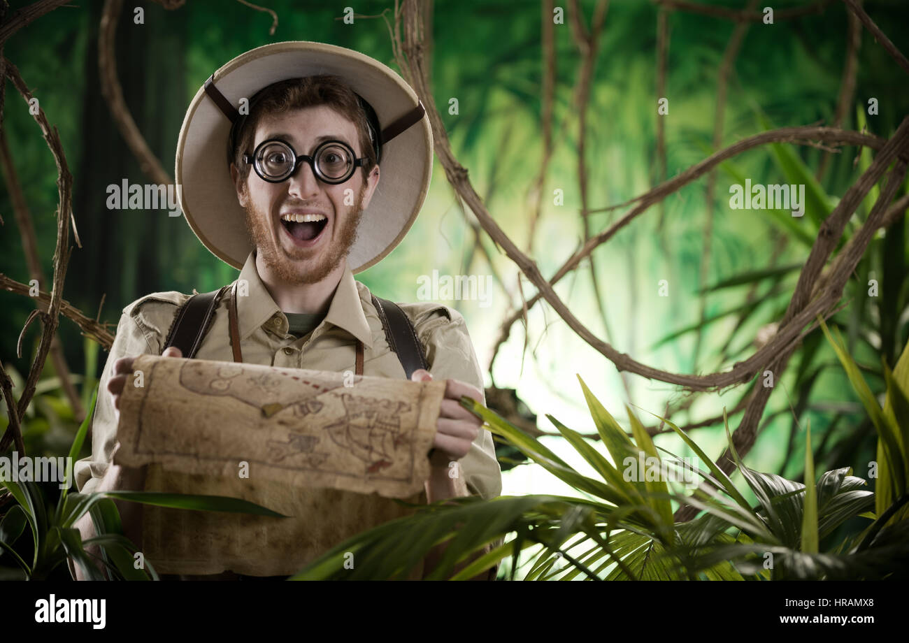 Young smiling explorer in the jungle with thick glasses holding a map ...
