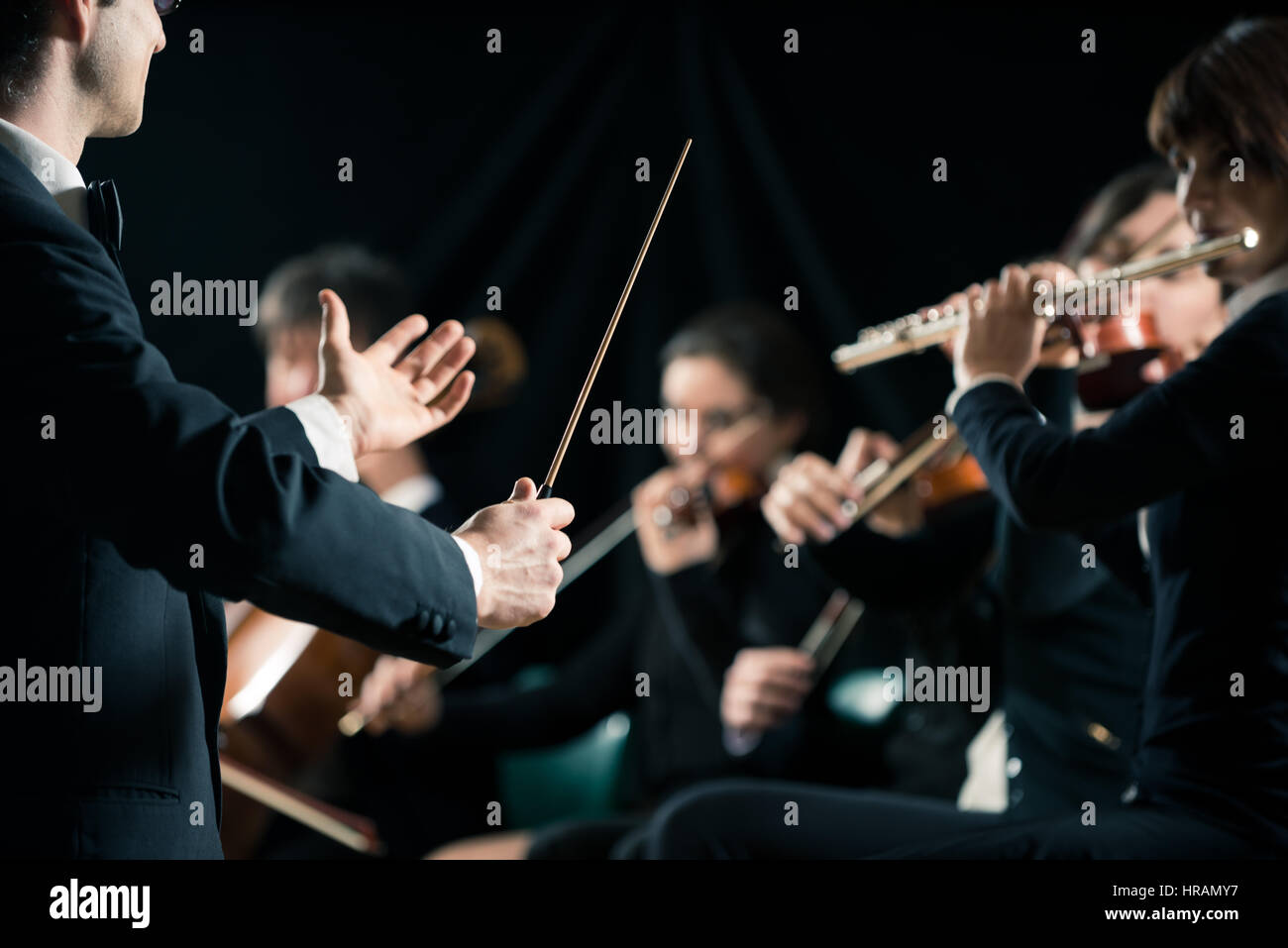 Conductor directing symphony orchestra with performers on background ...