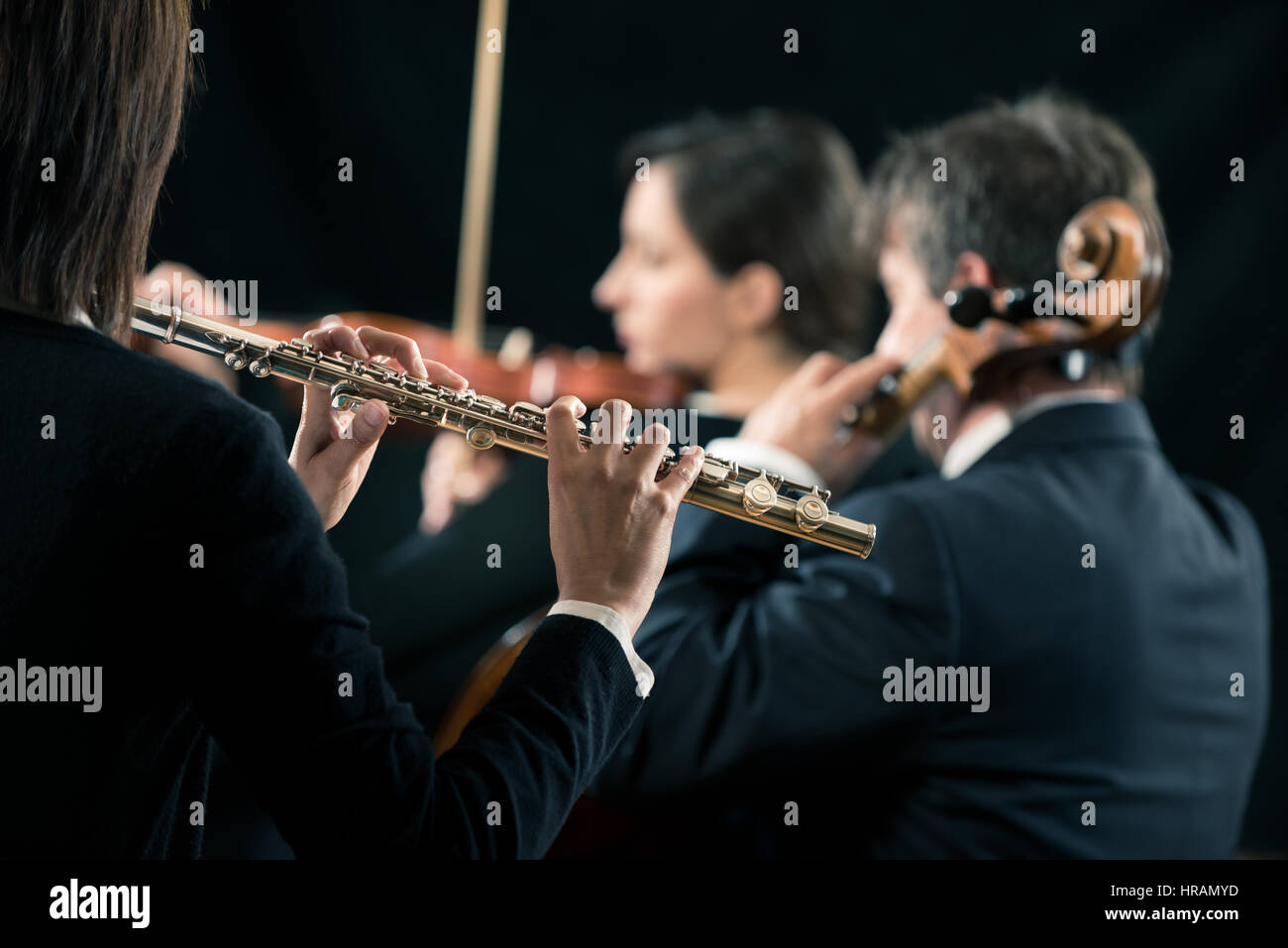 Professional female flutist in concert with symphony orchestra players ...