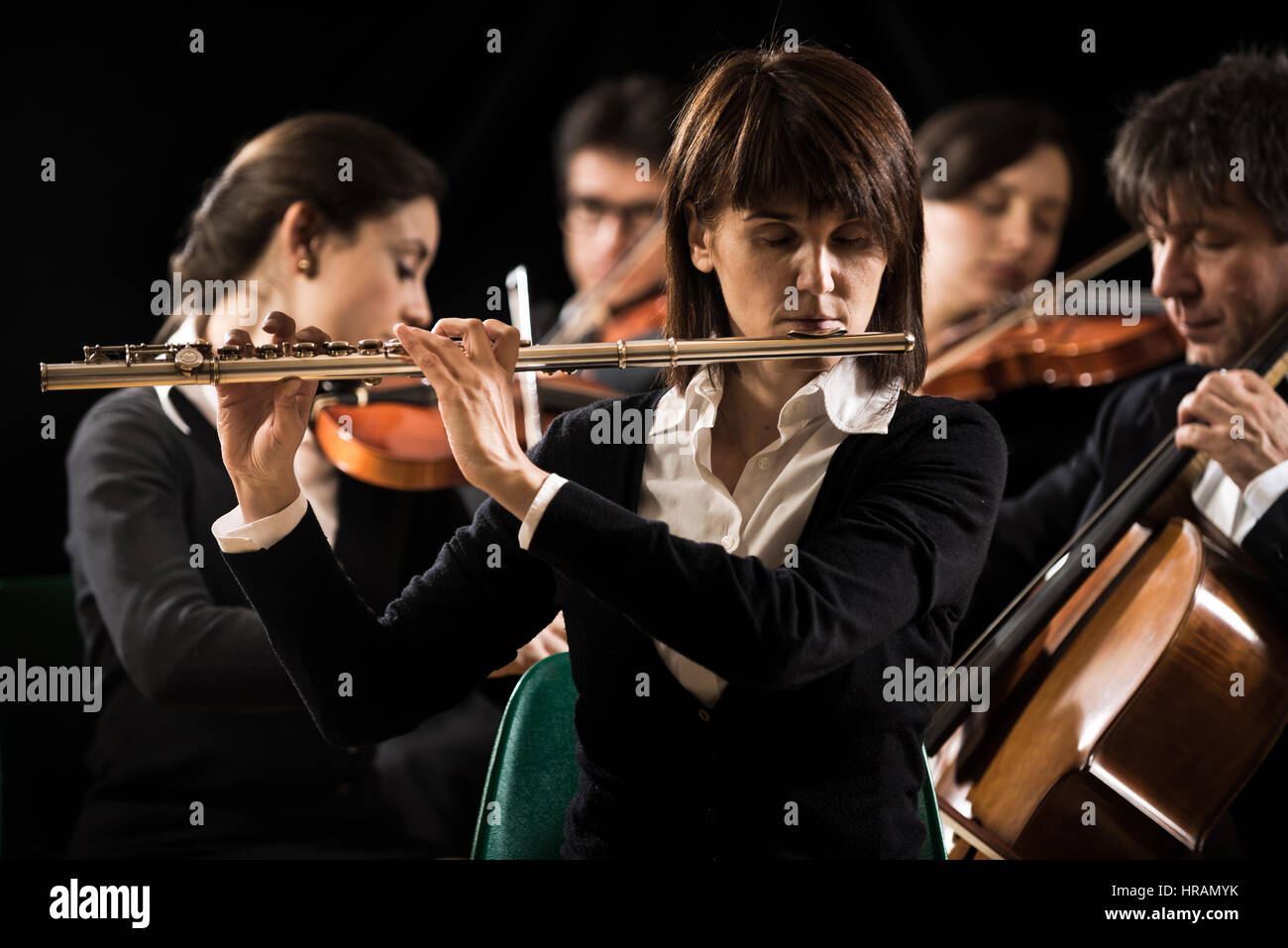 Professional female flutist in concert with symphony orchestra players ...