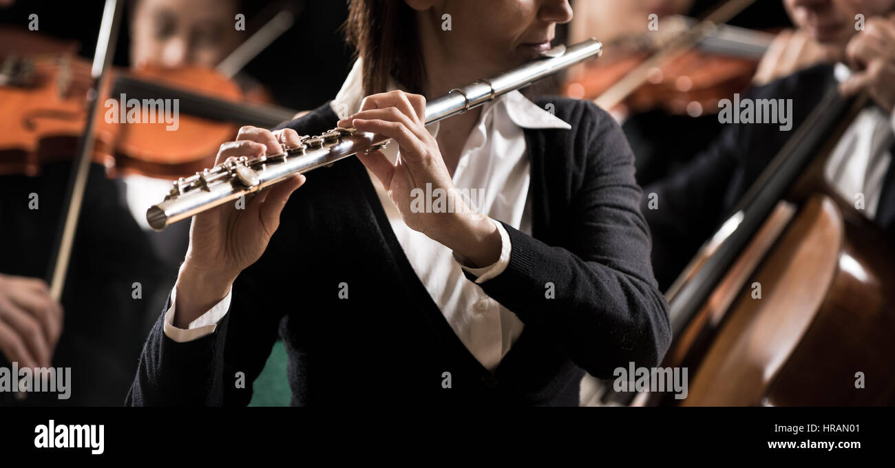 Professional female flutist in concert with symphony orchestra players ...