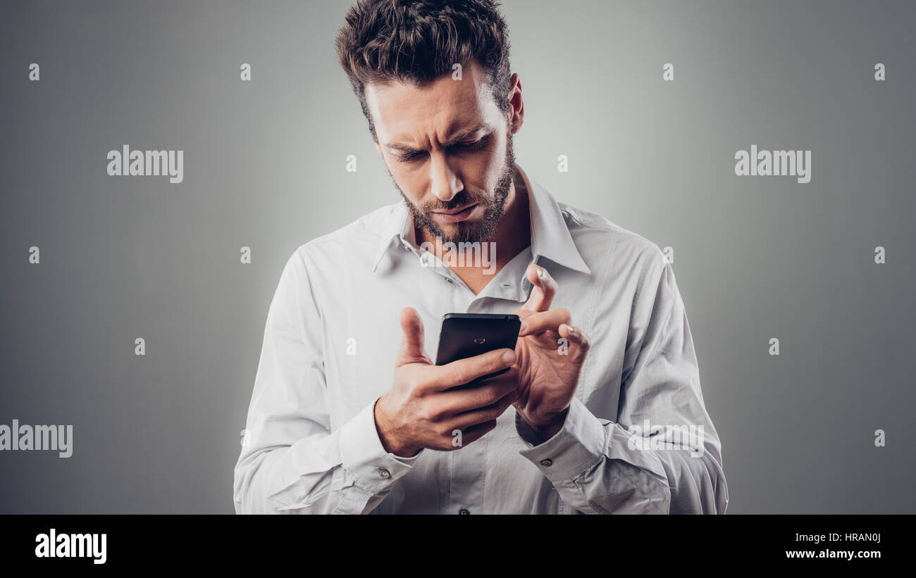Disappointed young man typing on his touch screen smartphone Stock ...
