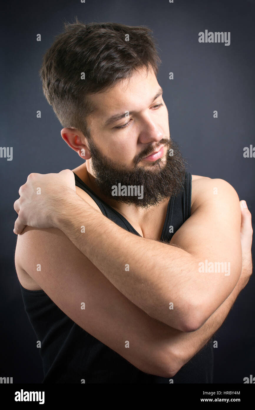 Lonely bearded man hugging himself against black background Stock Photo ...