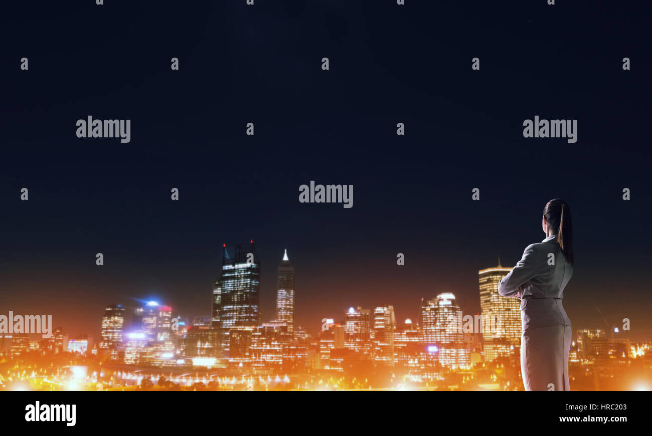 Rear view of elegant businesswoman viewing lights of night city Stock ...