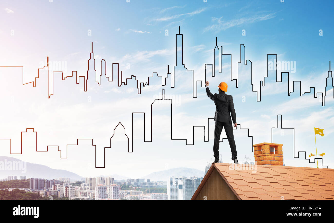Engineer man standing with back on house roof and drawing city. Mixed ...