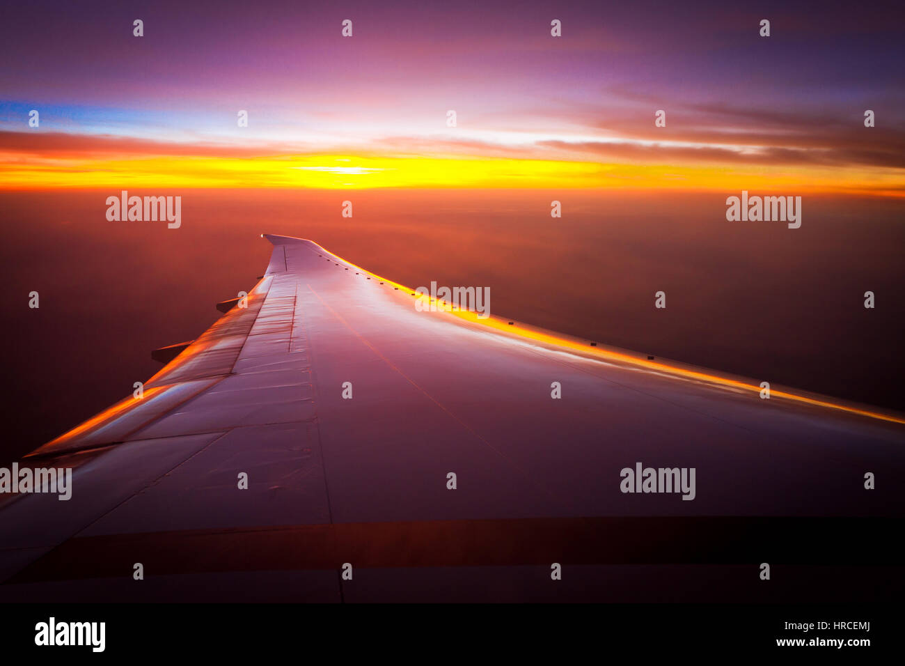 View along an airplane wing flying through a colorful orange sunset ...