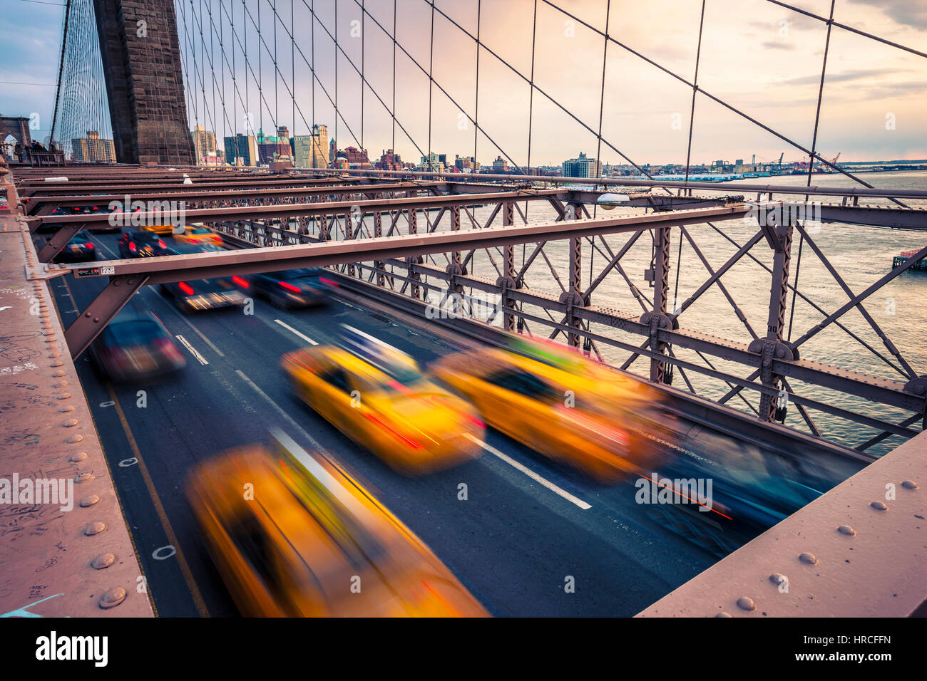 Yellow cab on Brooklyn Bridge in New York at cloudy sunset Stock Photo ...