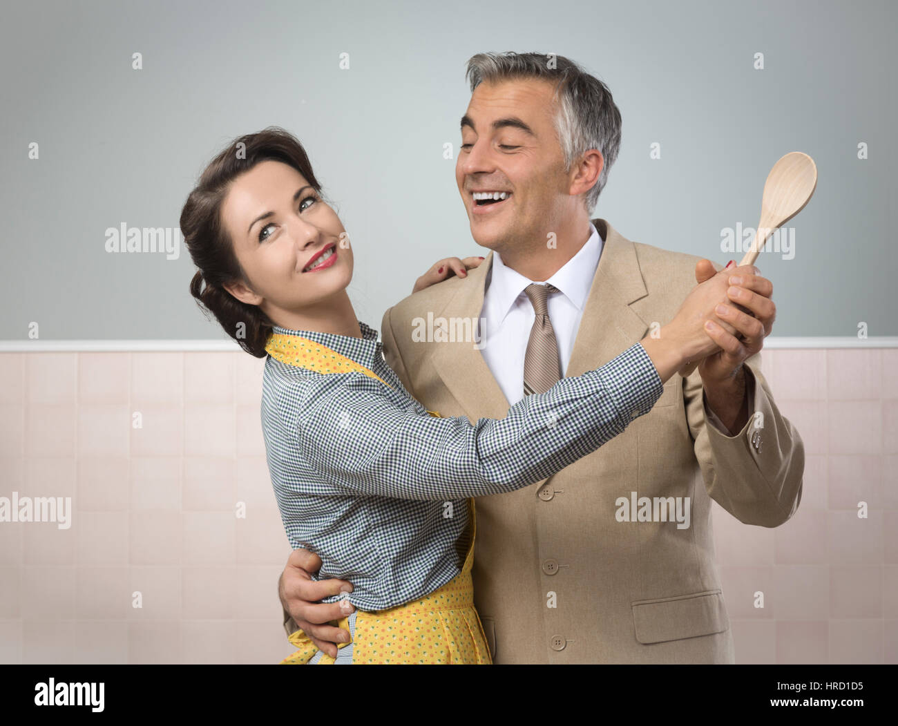 Smiling vintage couple dancing in the kitchen and holding a wooden ...