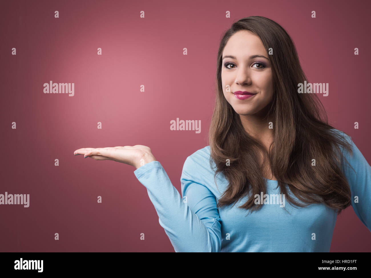 Smiling young woman presenting and displaying something at her side ...