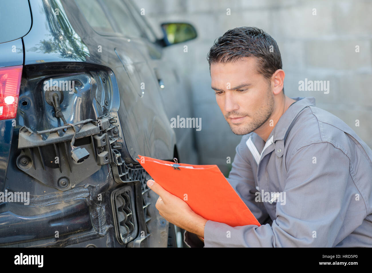 Mechanic holding clipboard assessing car Stock Photo - Alamy