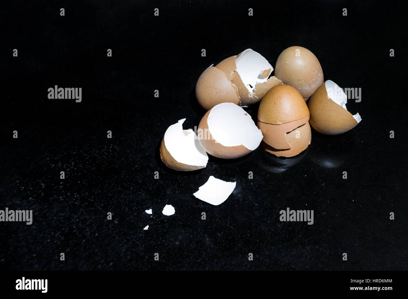 Broken egg shells pile up on dark kitchen table top. Close up with ...