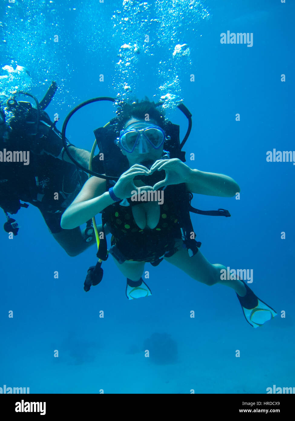 Underwater shoot of a young female diving with scuba and showing love ...