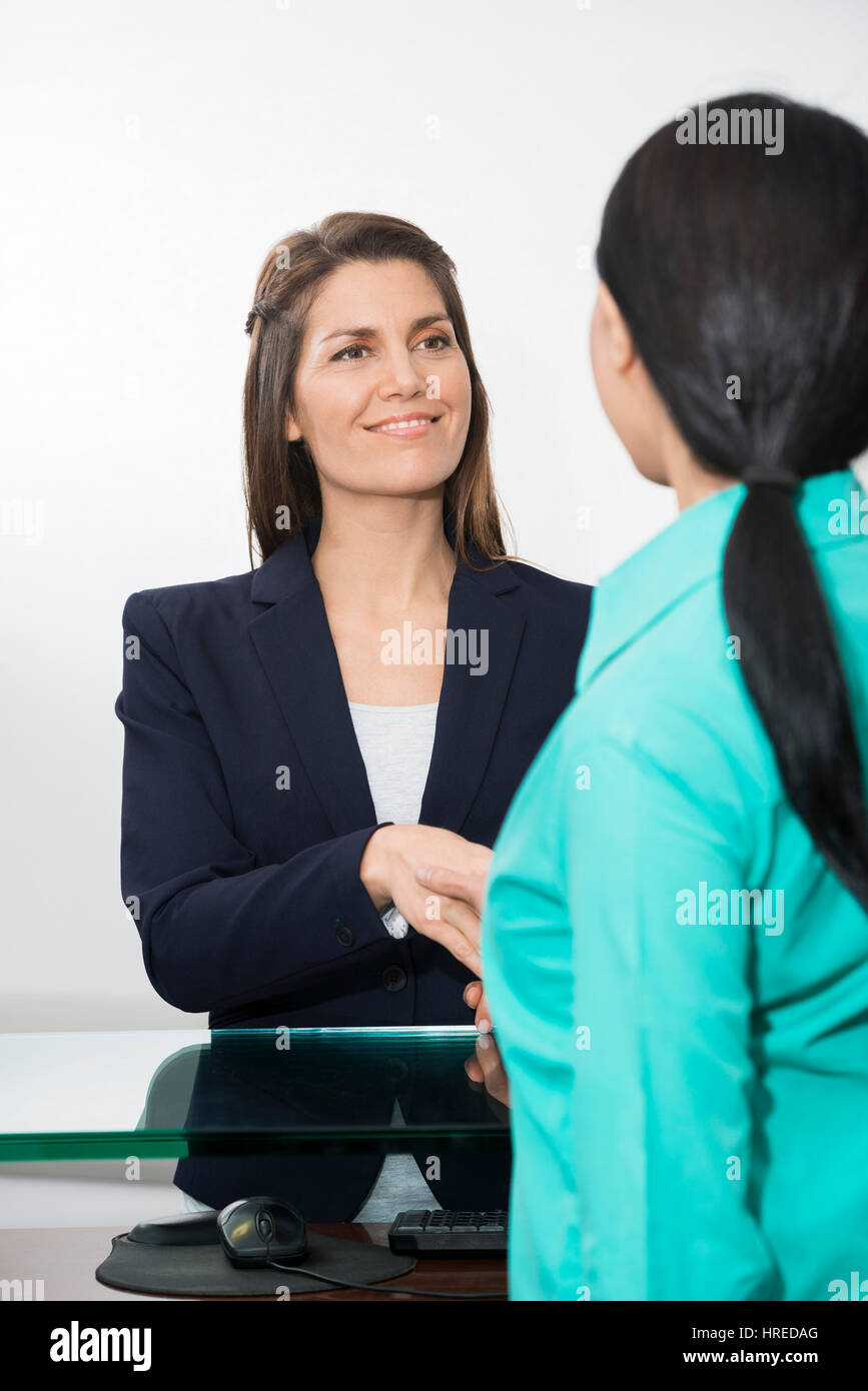 Happy female receptionist shaking hand with patient at desk in hospital ...