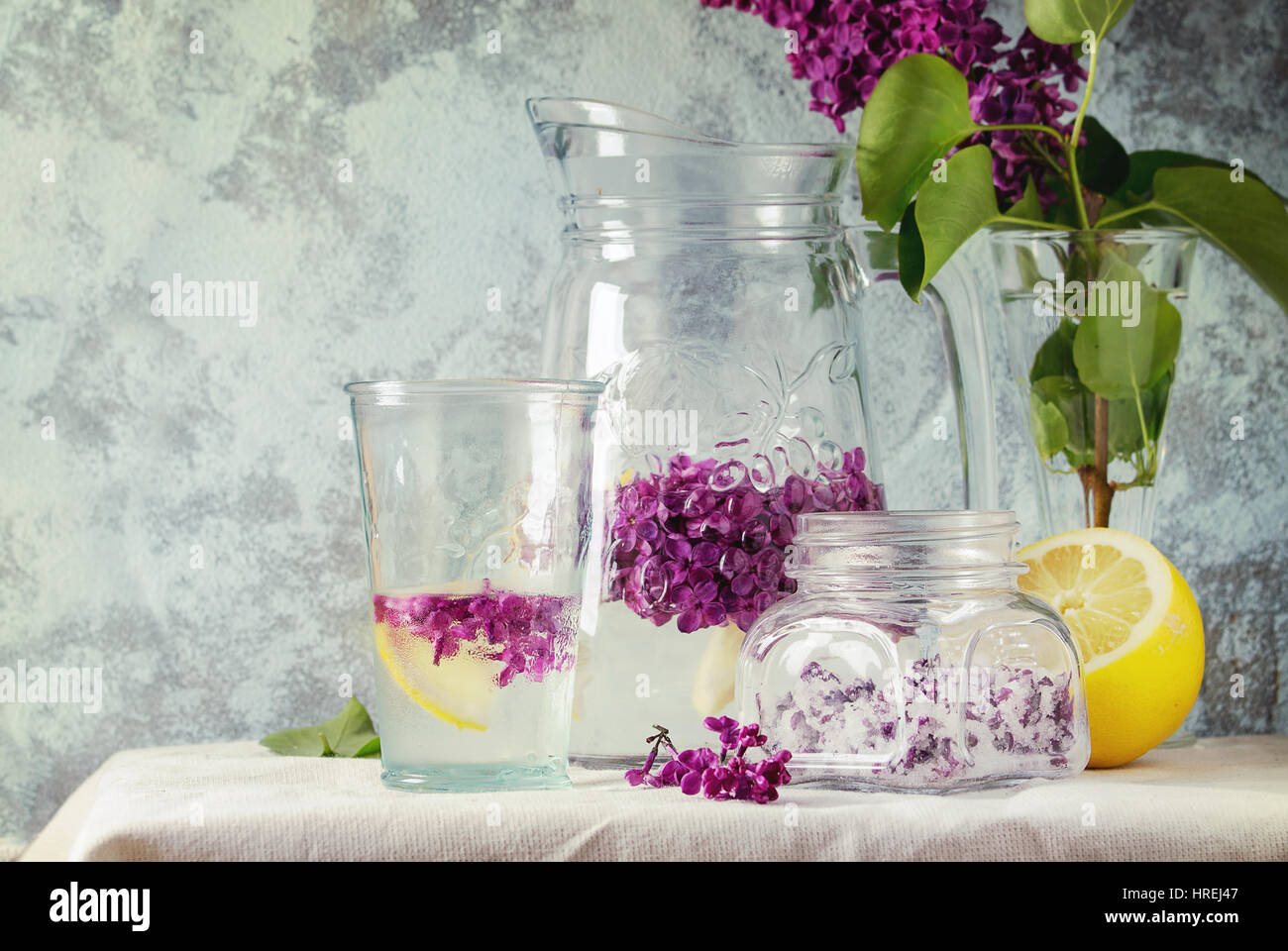 Glass jar of lilac flowers in sugar, glass and pitcher of lilac water ...