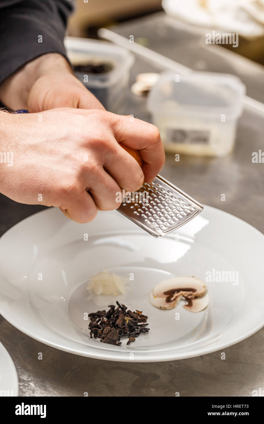 Chef rasping lemon zest over mushrooms, preparing his plate for soup ...