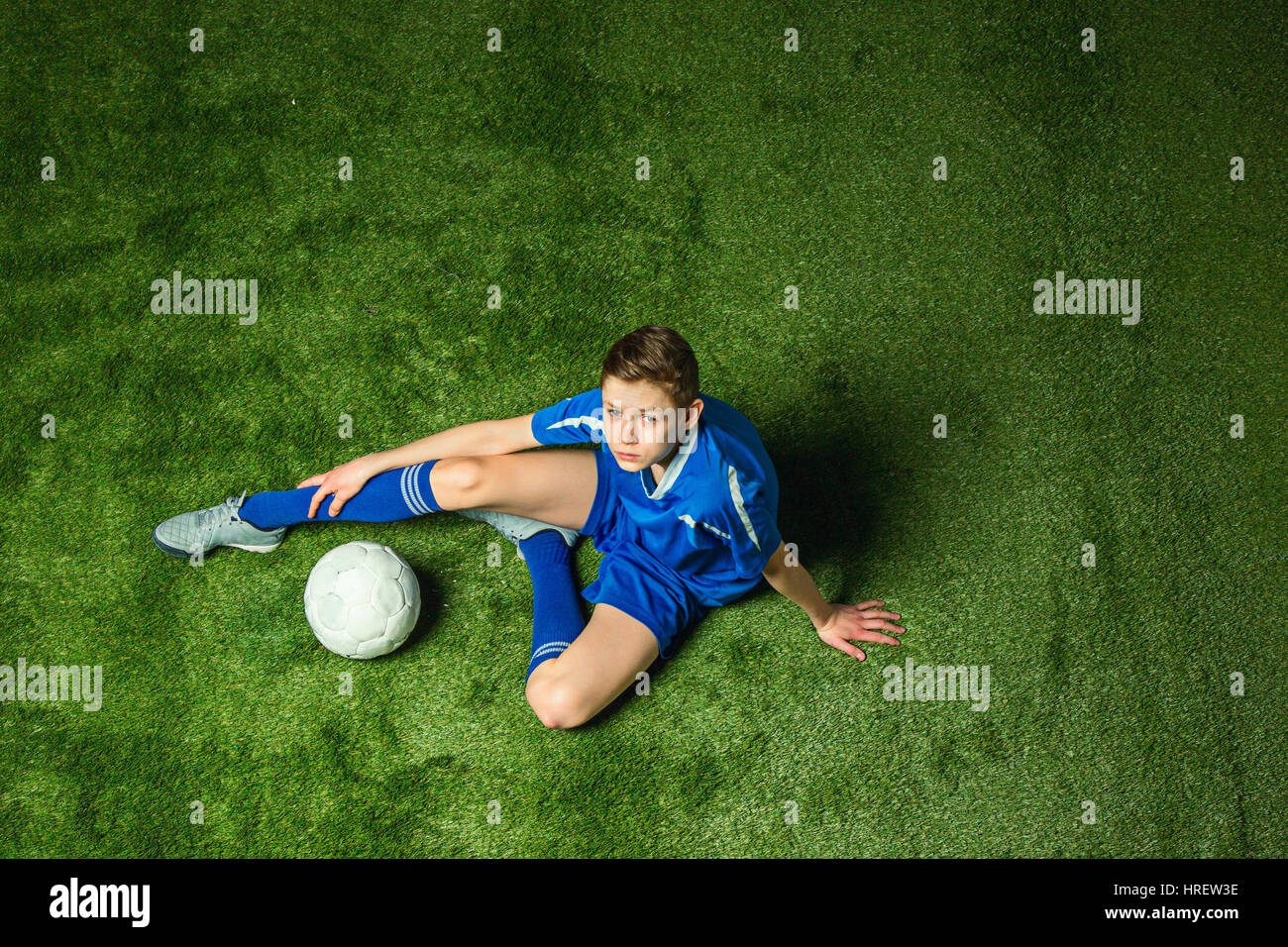 Boy soccer player sitting on green grass studio background as football ...