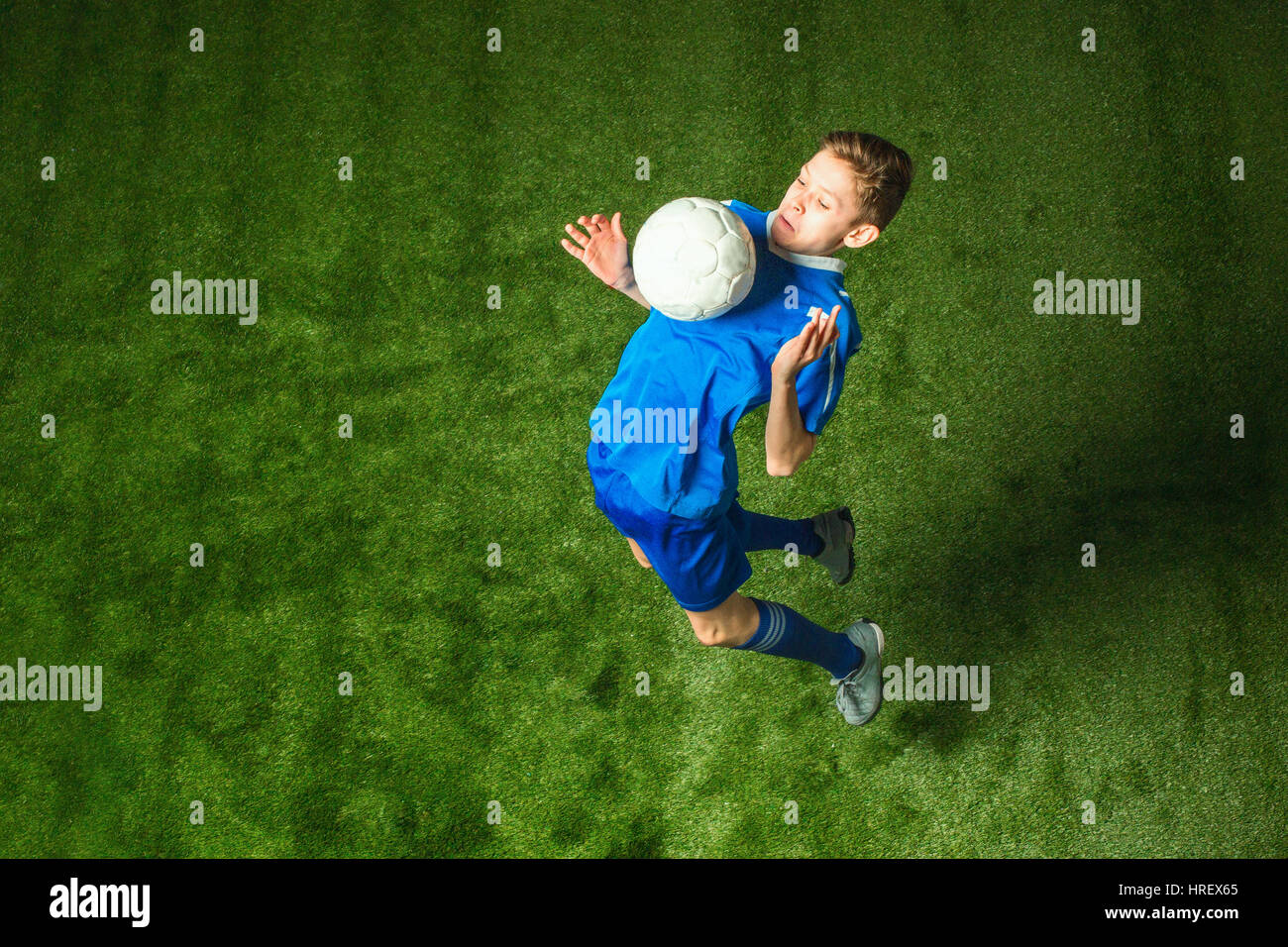 Young boy with soccer ball doing flying kick, on green studio ...