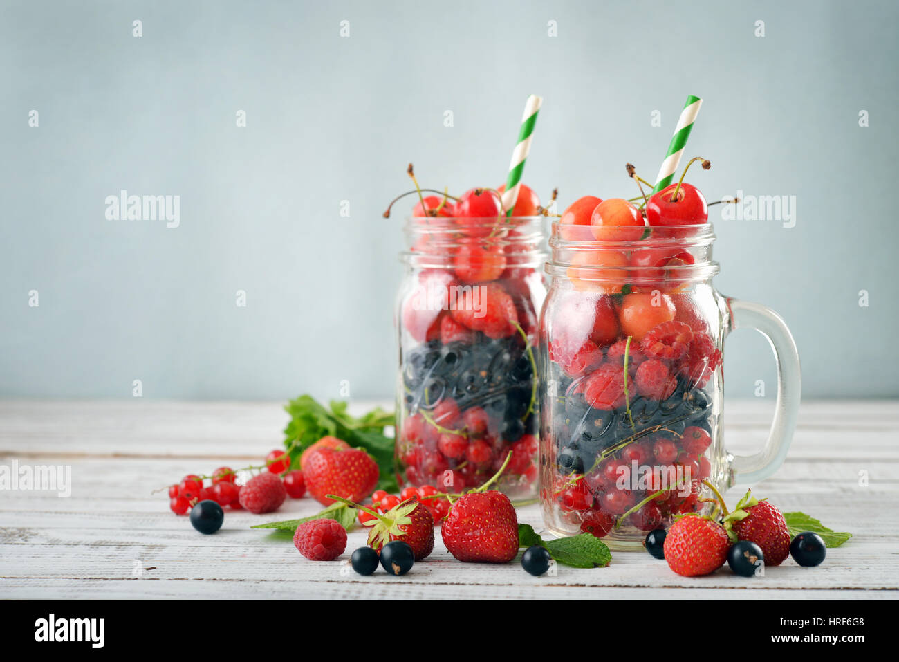 Different summer berries in glass jar with handle on wooden background ...