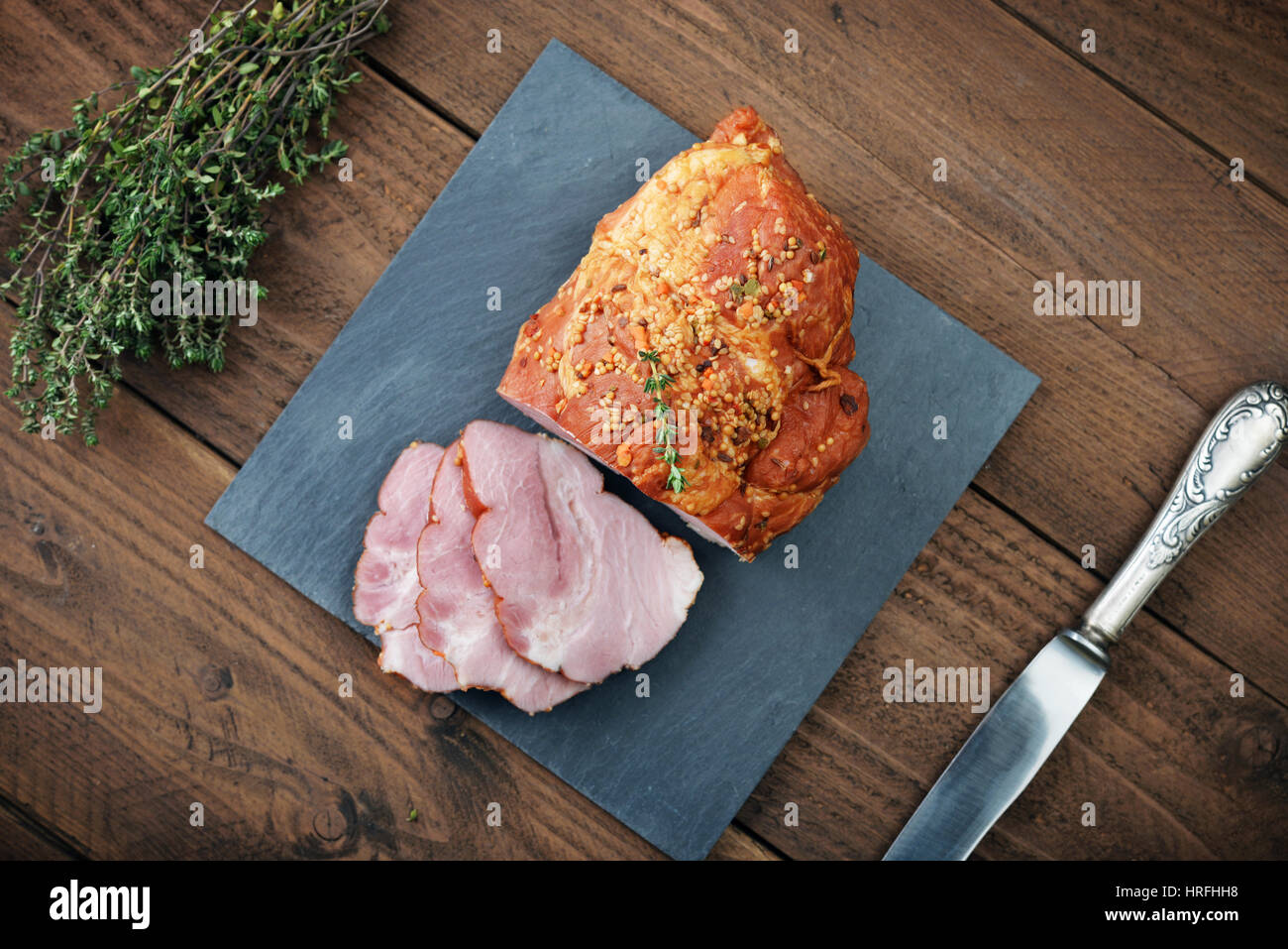 Sliced cold baked pork with herbs on a slate cutting board on wooden ...