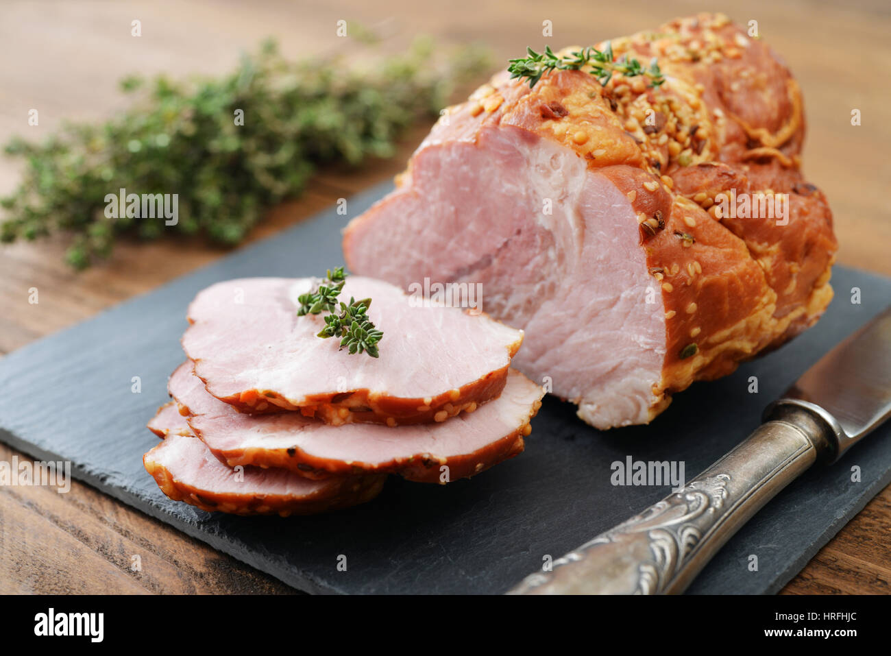 Sliced cold baked pork with herbs on a slate cutting board on wooden ...