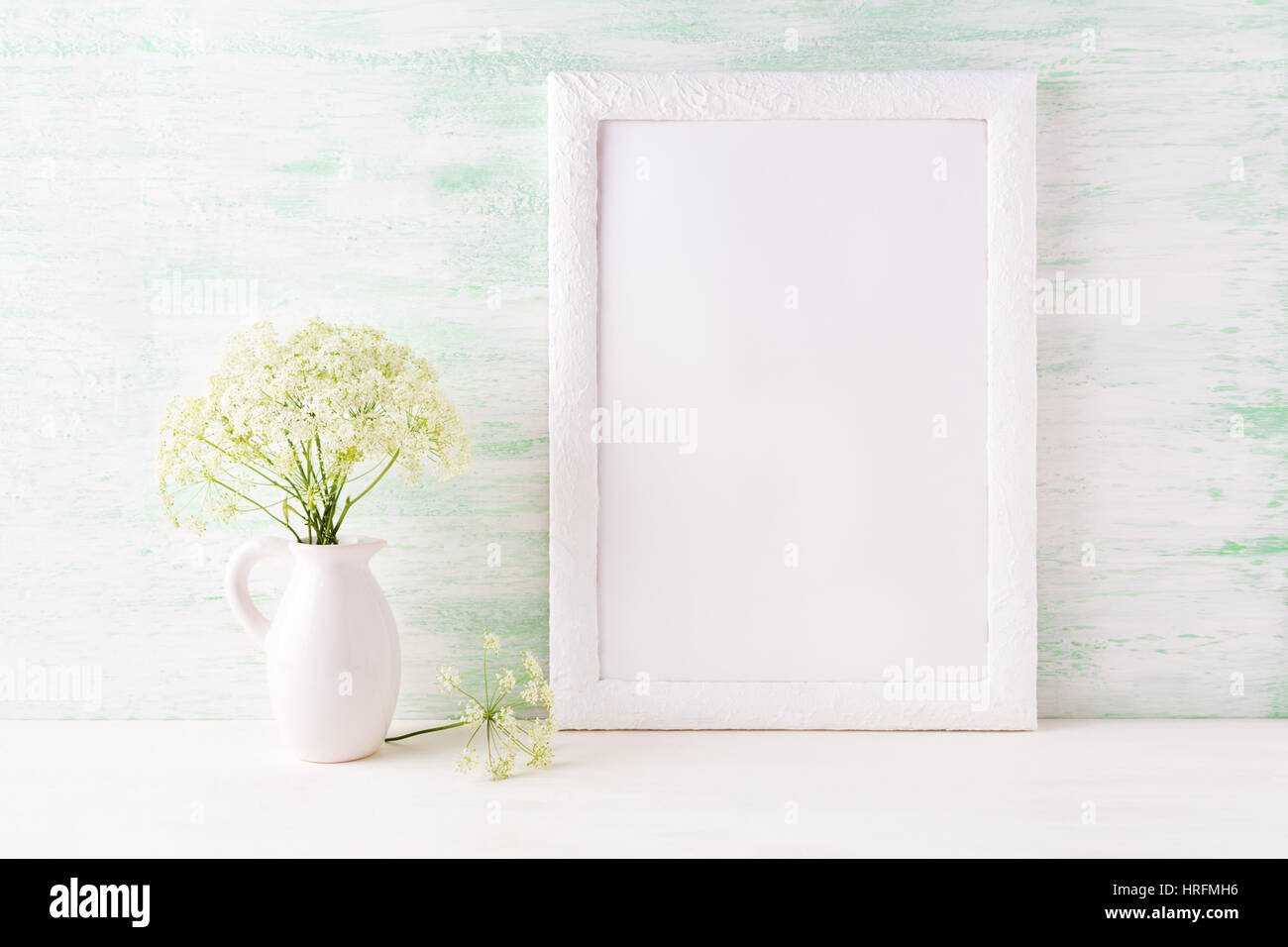 White frame mockup with delicate wild field flowers in pitcher. Empty ...