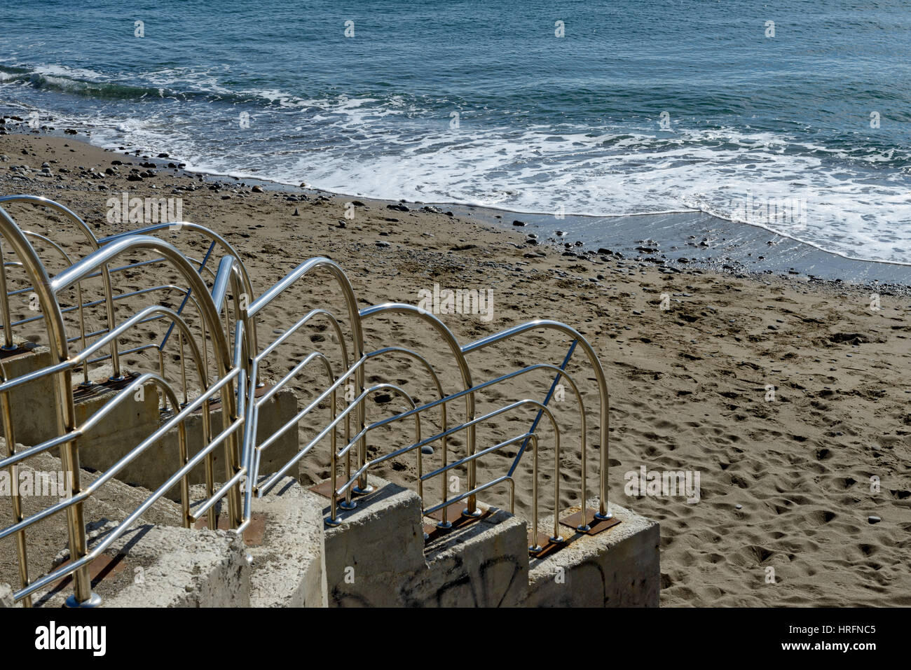 Shiny metal handrail of beach stair on background of sand and splashing ...