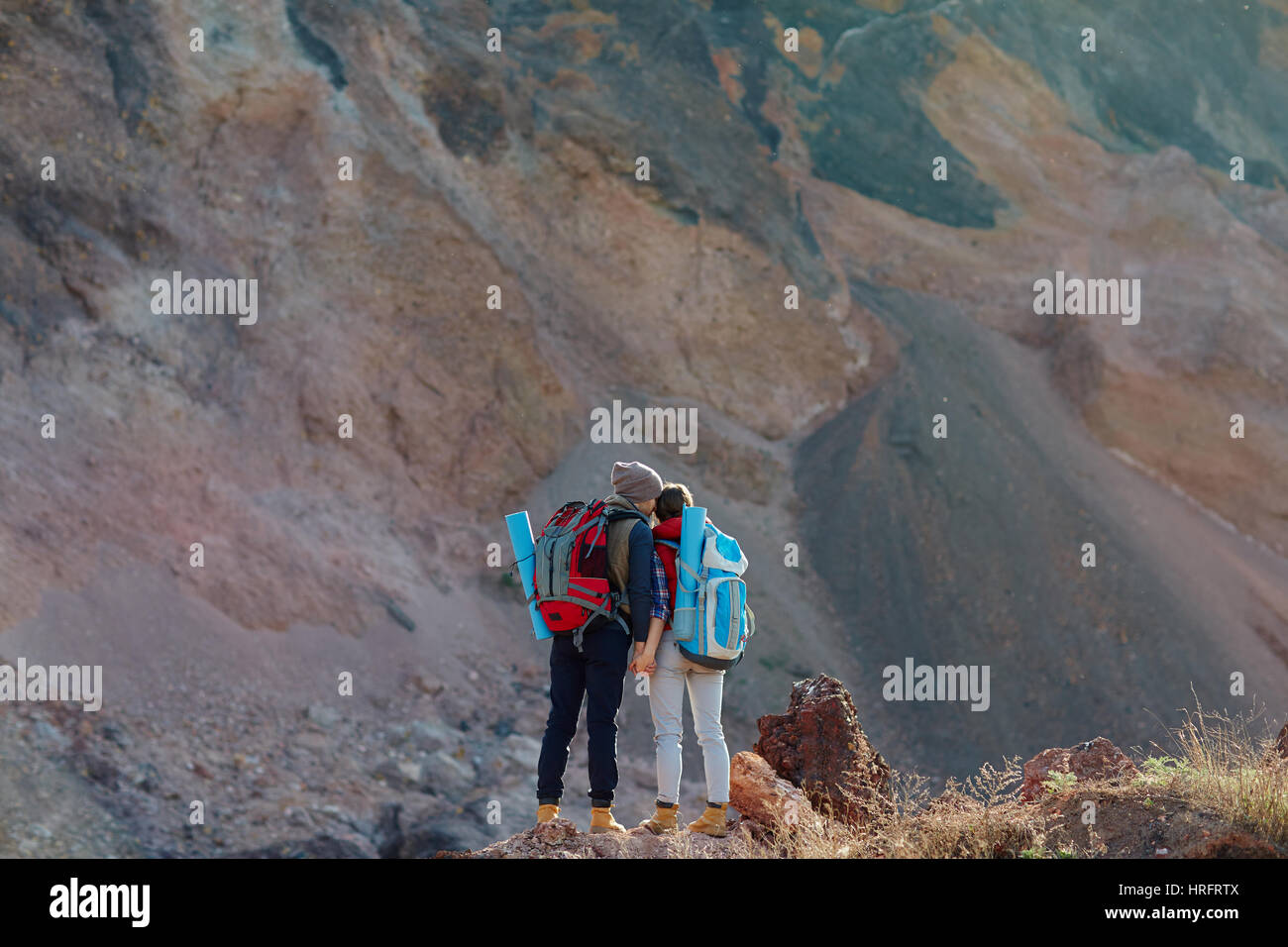 Rear view wide shot of loving tourist couple with big backpacks holding ...