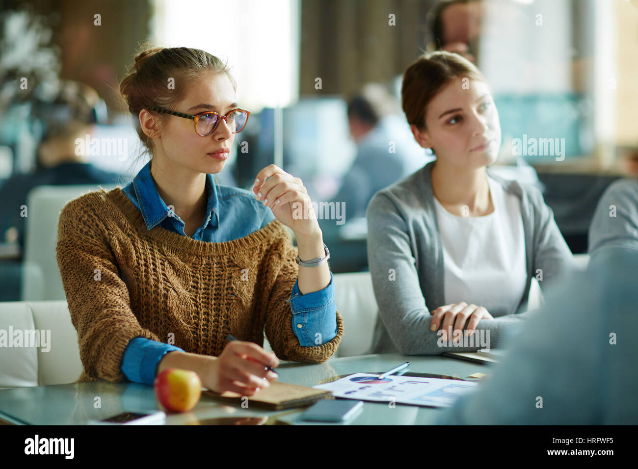 Two concentrated young women taking notes while having business ...