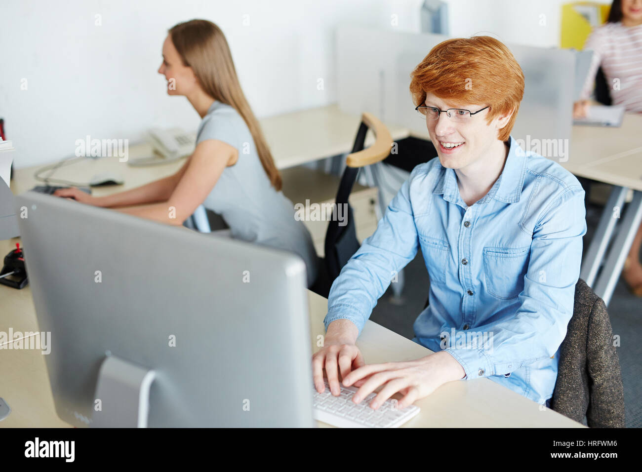 Young red-haired employee looking at computer screen with smile while ...