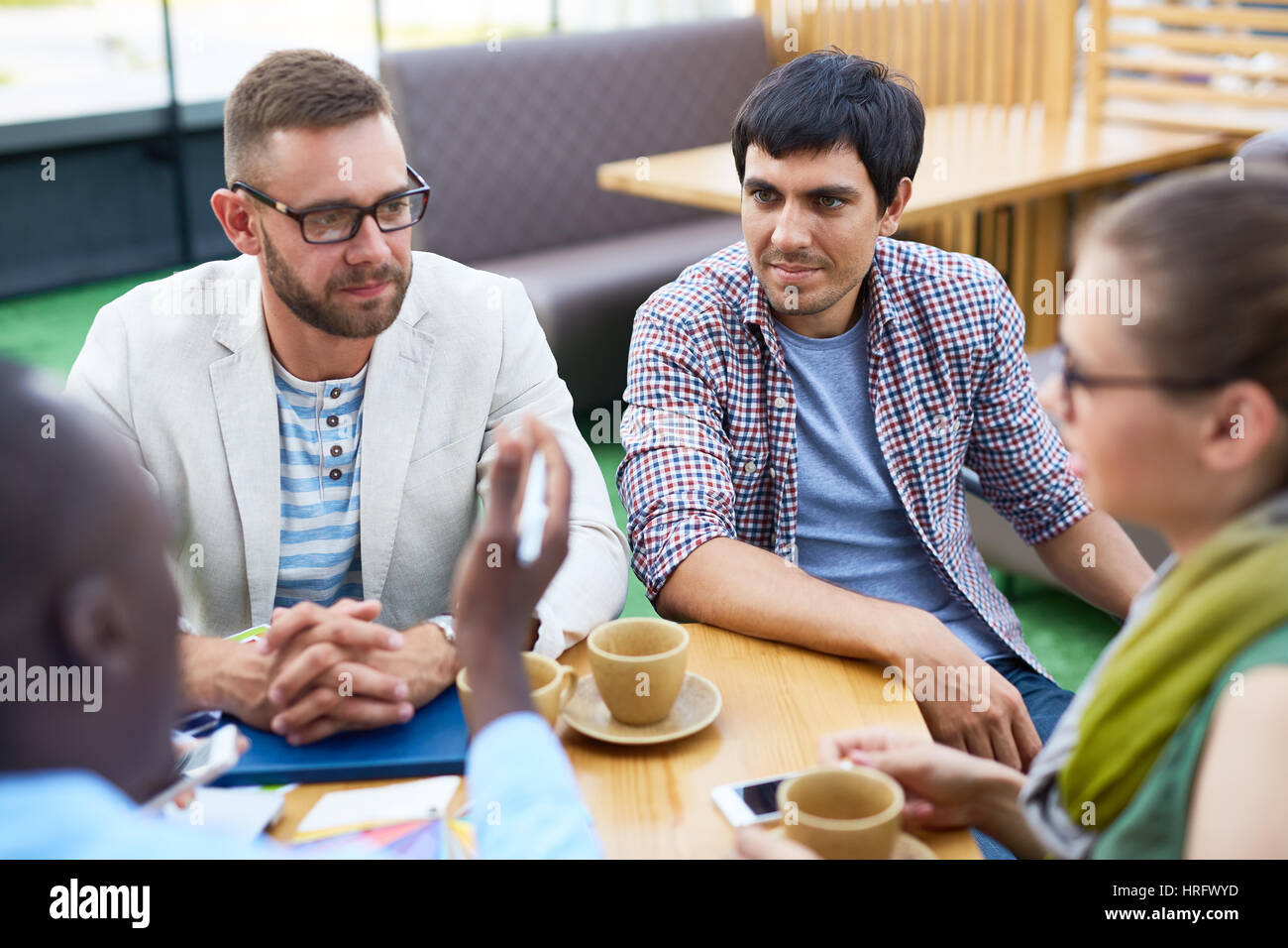 Group of creative young business people sitting at table in cafe and ...