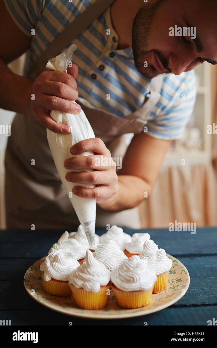 Portrait of male chef bending over kitchen table decorating freshly ...