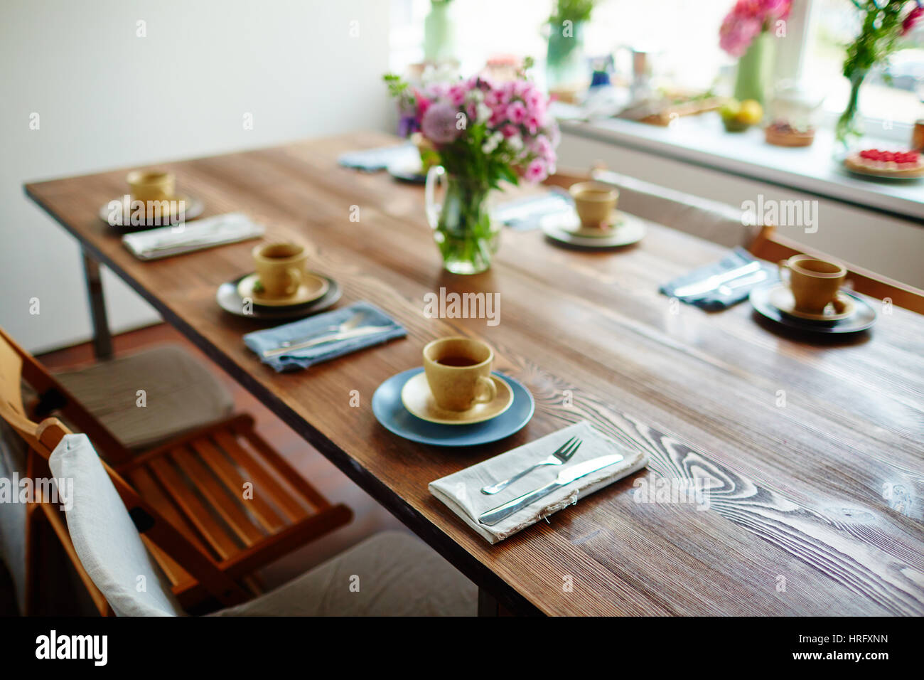Breakfast table setting with cups of tea, plates, cutlery and fresh-cut ...