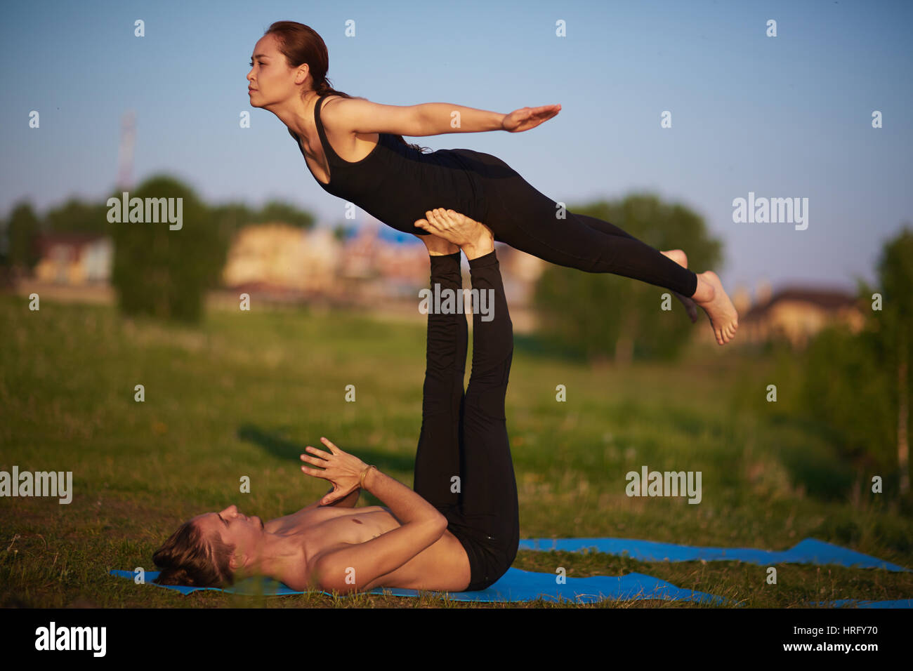 Young couple practicing front bird pose while doing acroyoga outdoors ...