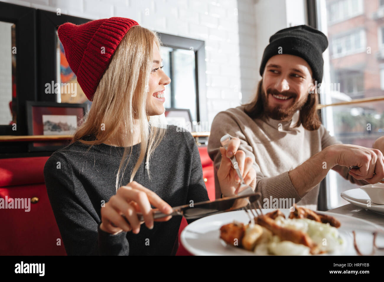 Side view of smiling couple sitting by the table and eating in cafe. As ...
