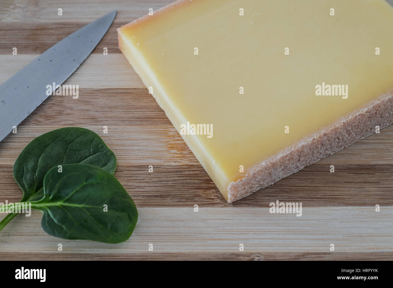 slice of french comte cheese on wood cutting board with fresh green ...