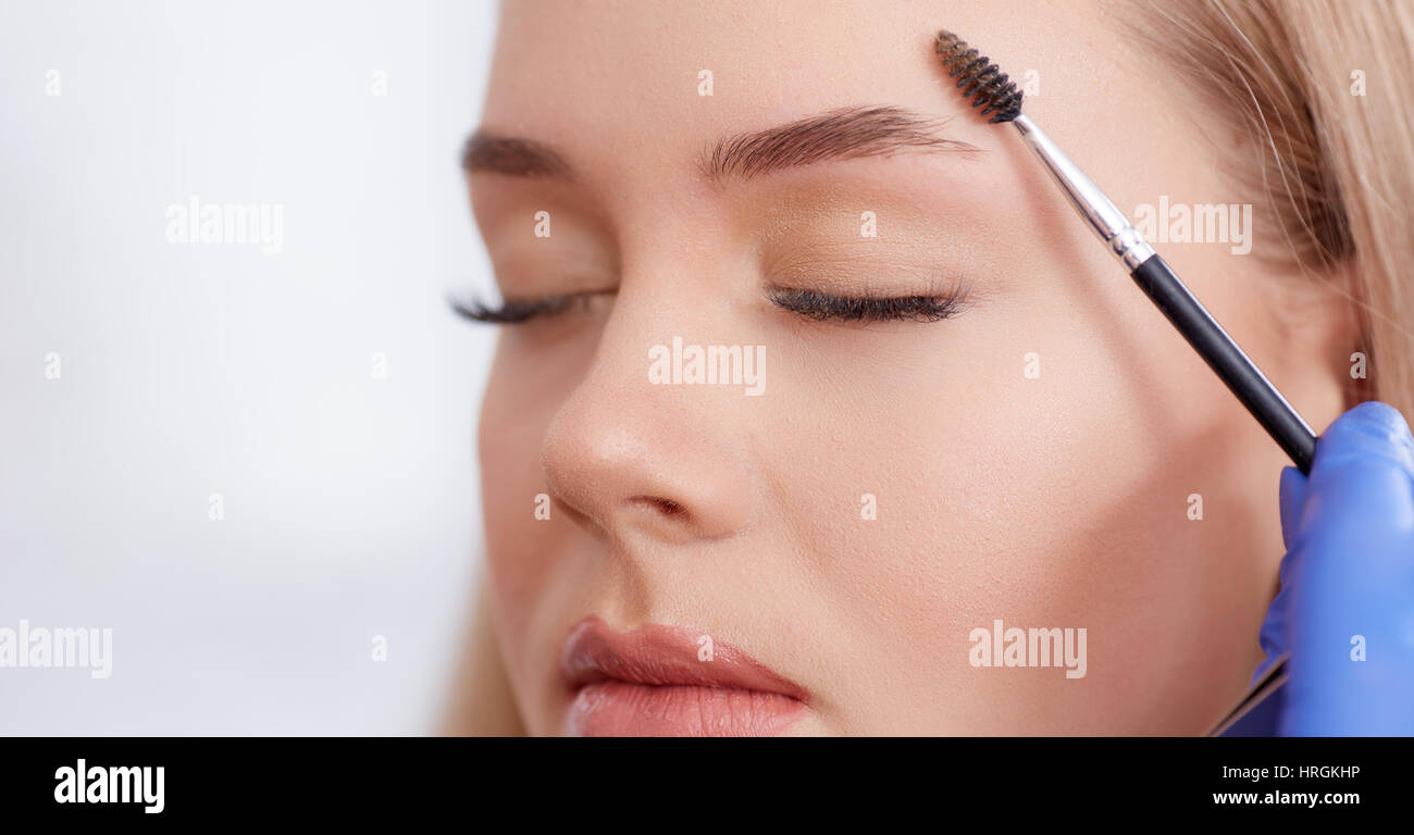 Professional cosmetologist in blue gloves combing eyebrows and ...