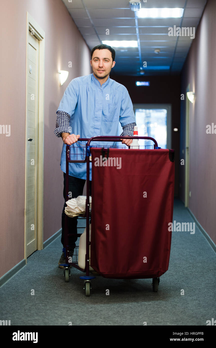 Young man pushing a housekeeping cart laden with clean towels, laundry ...