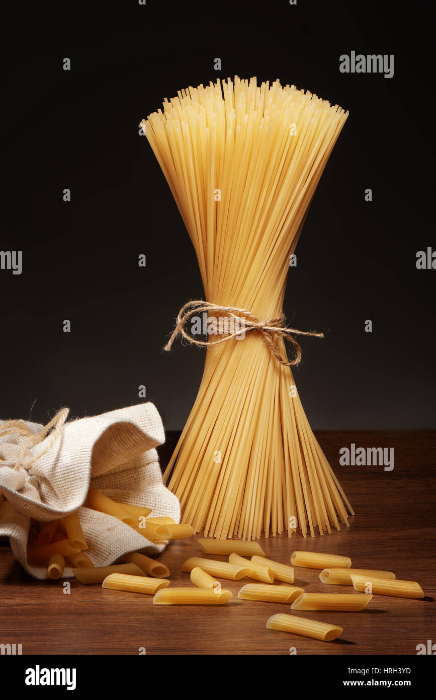 Dry spaghetti pasta tied up with rope and penne rigate pasta falling ...