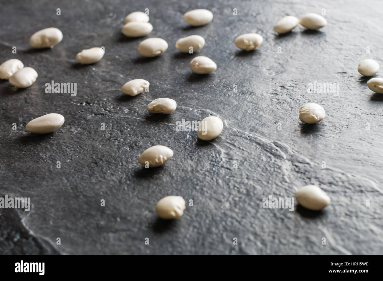 White beans are scattered randomly on a black stone table from slate ...
