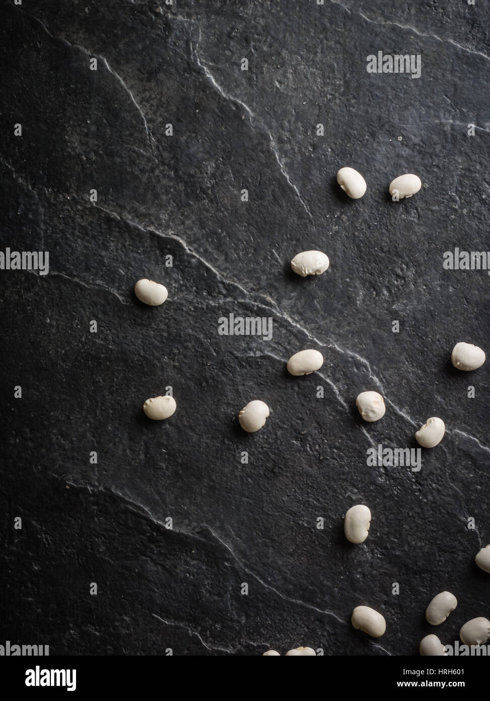 White beans are scattered randomly on a black stone table from slate ...